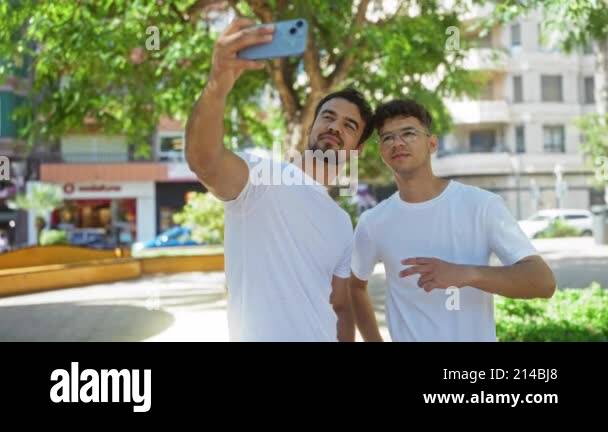 Two men taking a selfie together in an urban park on a sunny day ...
