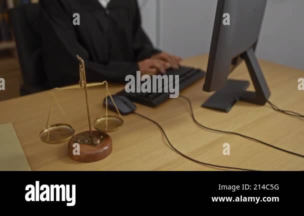 Woman judge working in office on computer with scales of justice on desk, showcasing a ...
