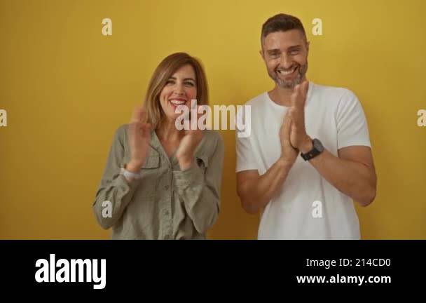 Man and woman clapping and smiling together against a yellow background ...