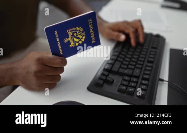 Young man in office holding cuban passport near computer keyboard ...