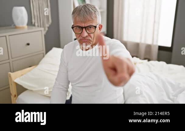 Angry middle age, grey-haired man in pyjamas stands in bedroom ...