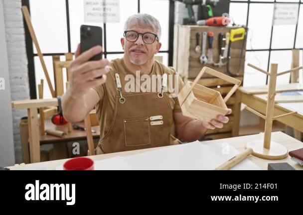 Middle-aged craftsman with grey hair video calling in a workshop ...