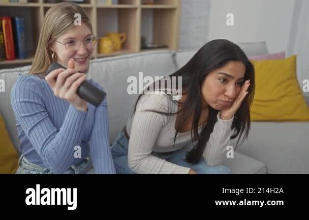 Two women friends express contrasting emotions in a modern apartment ...