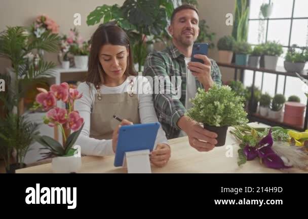 A woman and man collaborate in a flower shop, surrounded by plants ...