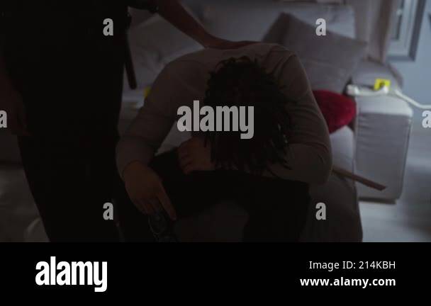 Woman officer monitoring handcuffed man sitting dejectedly in a dimly ...