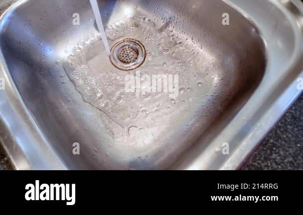 Footage of water from a faucet running in slow motion into a kitchen ...