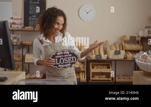Two women holding open and closed signs in a bakery with bread and ...