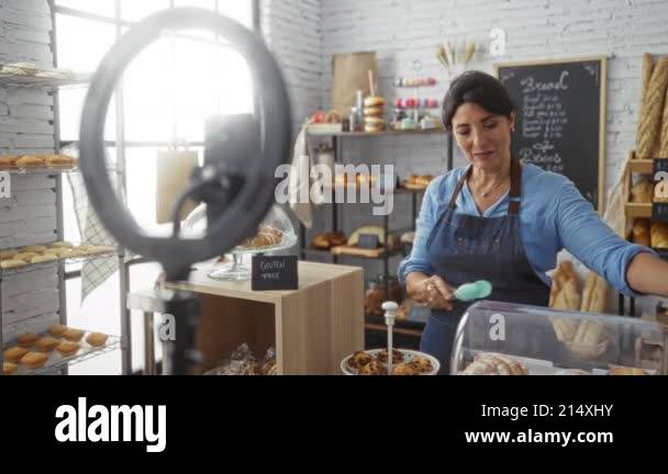 Woman preparing pastries in a bakery while recording a video for social media, showcasing a ...