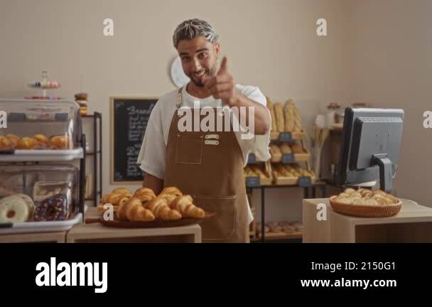 Young man smiling in bakery shop with croissants and other pastries in ...
