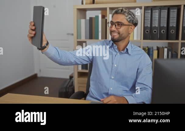 Young arab man taking selfie on tablet in office workplace, wearing ...