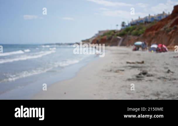 Blurry beach scene featuring people by the ocean with cliffs and houses ...