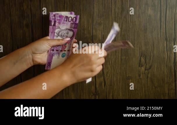 Woman counting philippine peso bills with hands on a wood background ...