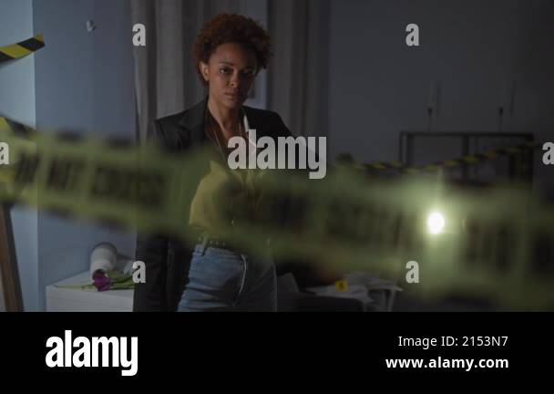 A focused woman detective investigates a crime scene indoors, gun ready ...