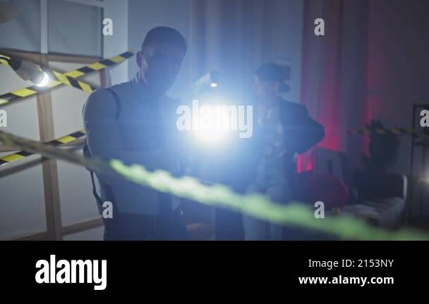 A man and a woman investigating a dimly lit indoor crime scene with ...