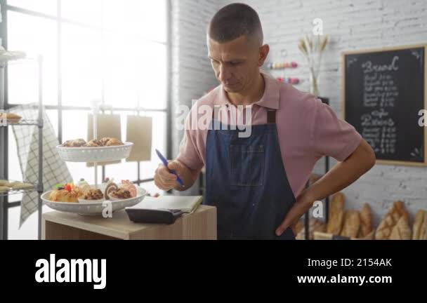Young man writing in notebook while working in a bakery surrounded by ...