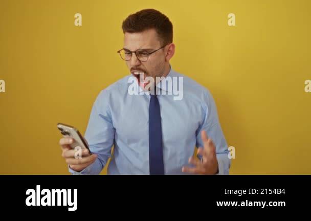 Angry young hispanic man in shirt and tie screaming into smartphone ...