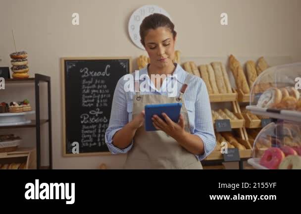 Young woman working in a bakery using a tablet surrounded by bread and ...