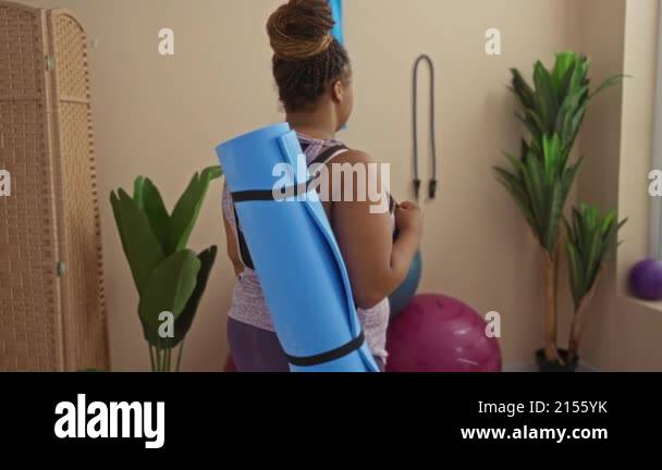 Woman preparing for workout at the gym carrying a blue yoga mat ...