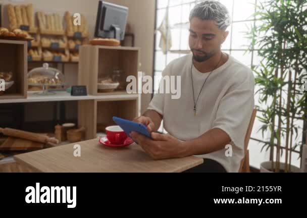 Young man drinking coffee and using tablet in a bakery shop interior ...
