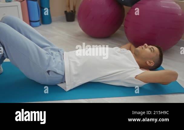 Young man exercising on a blue mat indoors at a gym center, surrounded ...