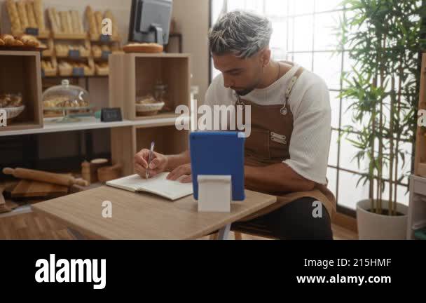 Young man with beard writing in a notebook and looking at a computer ...