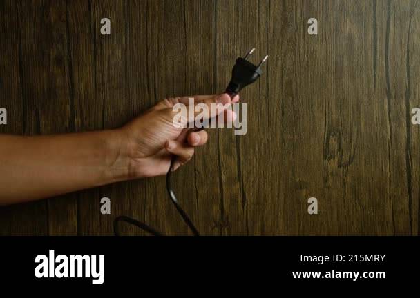 Man holding black electrical plug against wooden background ...