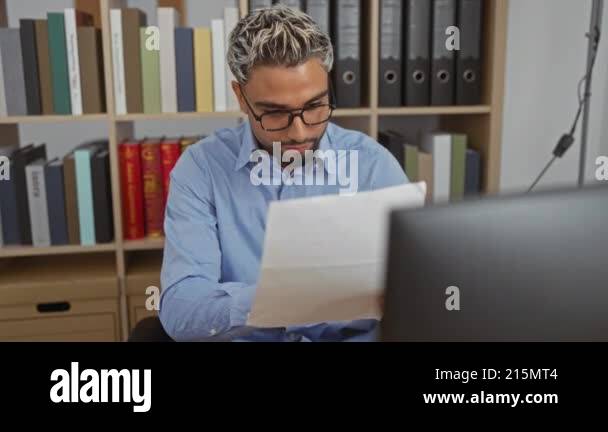 Young man reading documents in an office, appearing focused and later ...