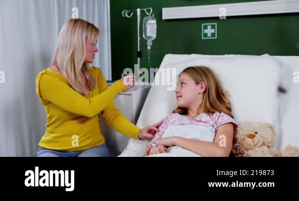 A mother lovingly supports her sick daughter in a hospital room ...