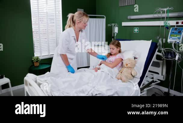 A nurse checks in on a young girl in her hospital room, offering ...