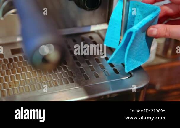 A hand is using a blue cloth to meticulously clean an espresso machine ...