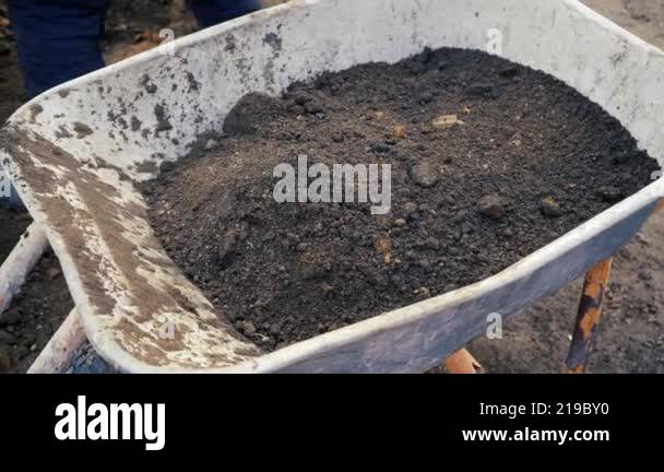 A worker pours soil into a wheelbarrow with a shovel close-up 4K ...