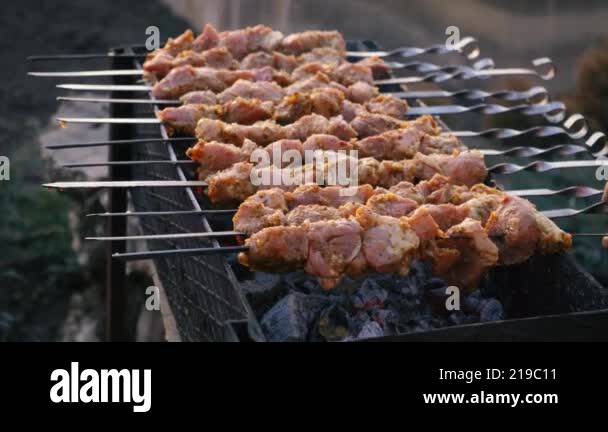 A man cooks barbecue on skewers on charcoal grill on the street. Barbecue outdoor. Picnic in ...