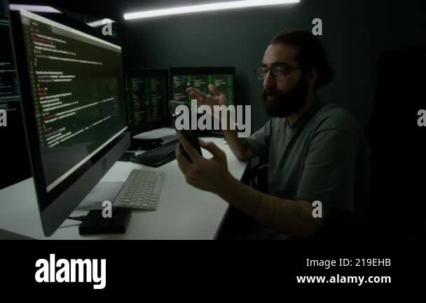 Long-haired, bearded programmer talking via video call with his colleague, consulting about ...
