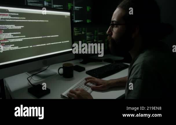 Bearded Programmer Writing Code Sitting At Desk With Multiple Monitor Screens Displaying