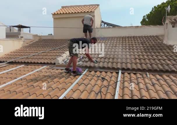 Workers on a red-tiled roof cutting and preparing mounting areas for ...