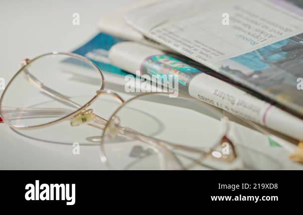 A close up of the glasses lying next to a stack of newspaper. Moving ...
