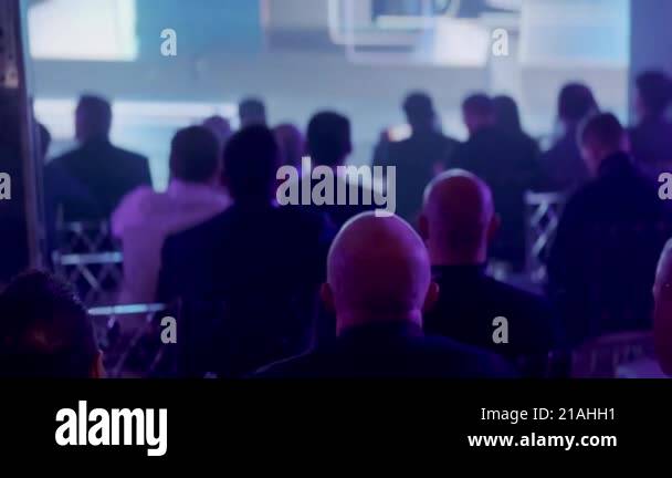Group of people in a conference room seated facing a stage with blue ...