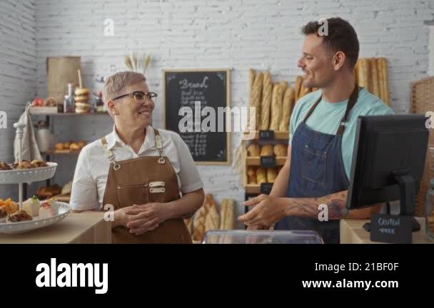 Woman and man workers smiling and talking in a bakery shop with bread ...