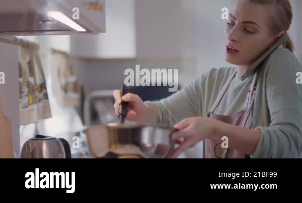A busy woman talks on the phone while frying food and preparing meals ...