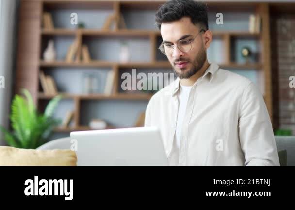 Handsome man working typing on a laptop sitting on ofa in living room ...