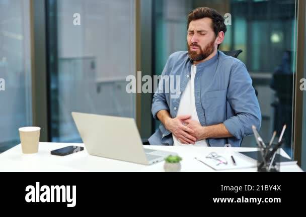 Bearded man experiencing sudden, severe stomach pain while working at ...