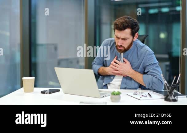 Worried businessman clutching chest in pain while working on laptop in ...