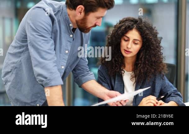 Focused colleagues discuss a document in a bright office. Business woman with curly hair and ...