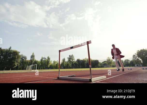 Businessman jumping a hurdle while running on the athletics racing ...