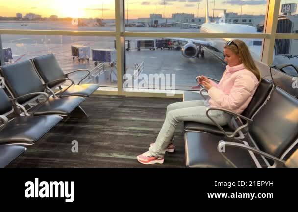 A woman is seated in an airport waiting area, gazing thoughtfully out the window, where she ...