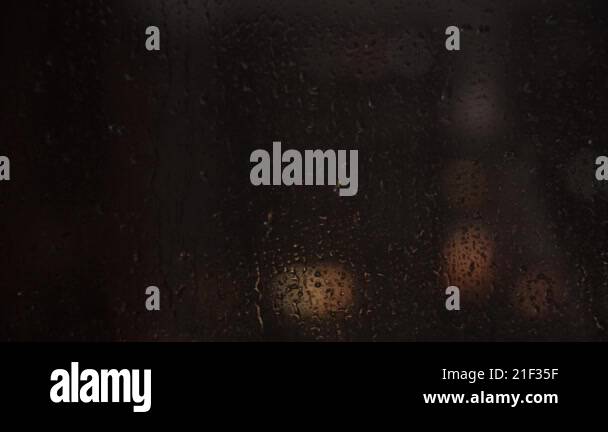 Raindrops on a glass window at night, with warm blurred lights creating ...