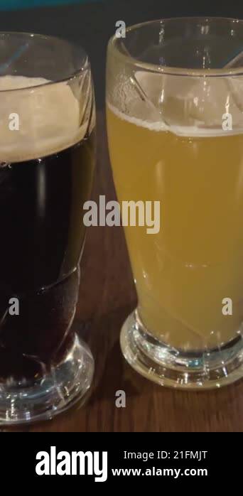 Beer is pouring into a two beer mugs with bubbles close-up on a black ...