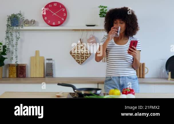Young happy multiracial woman using mobile phone while cooking in the ...