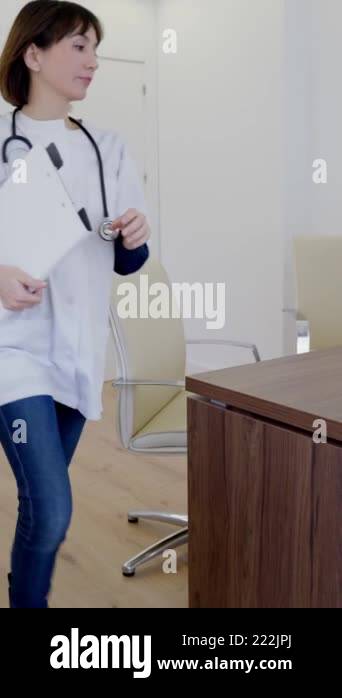 Professional female doctor walks to her desk and starts working on her ...