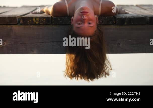 A woman lies back on a wooden pier with her head dangling over the edge ...